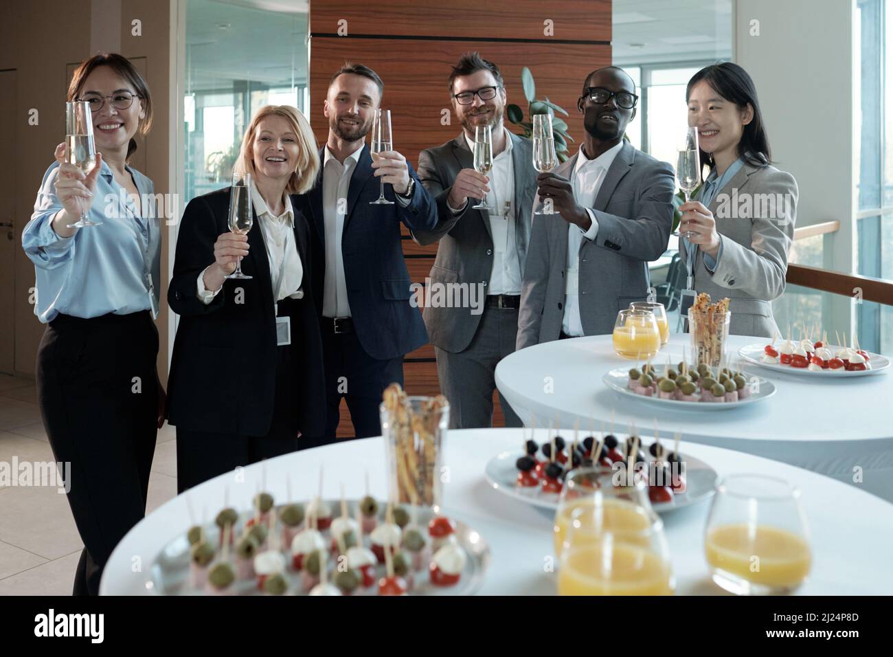 Group of cheerful business team in formalwear toasting at buffet in ...