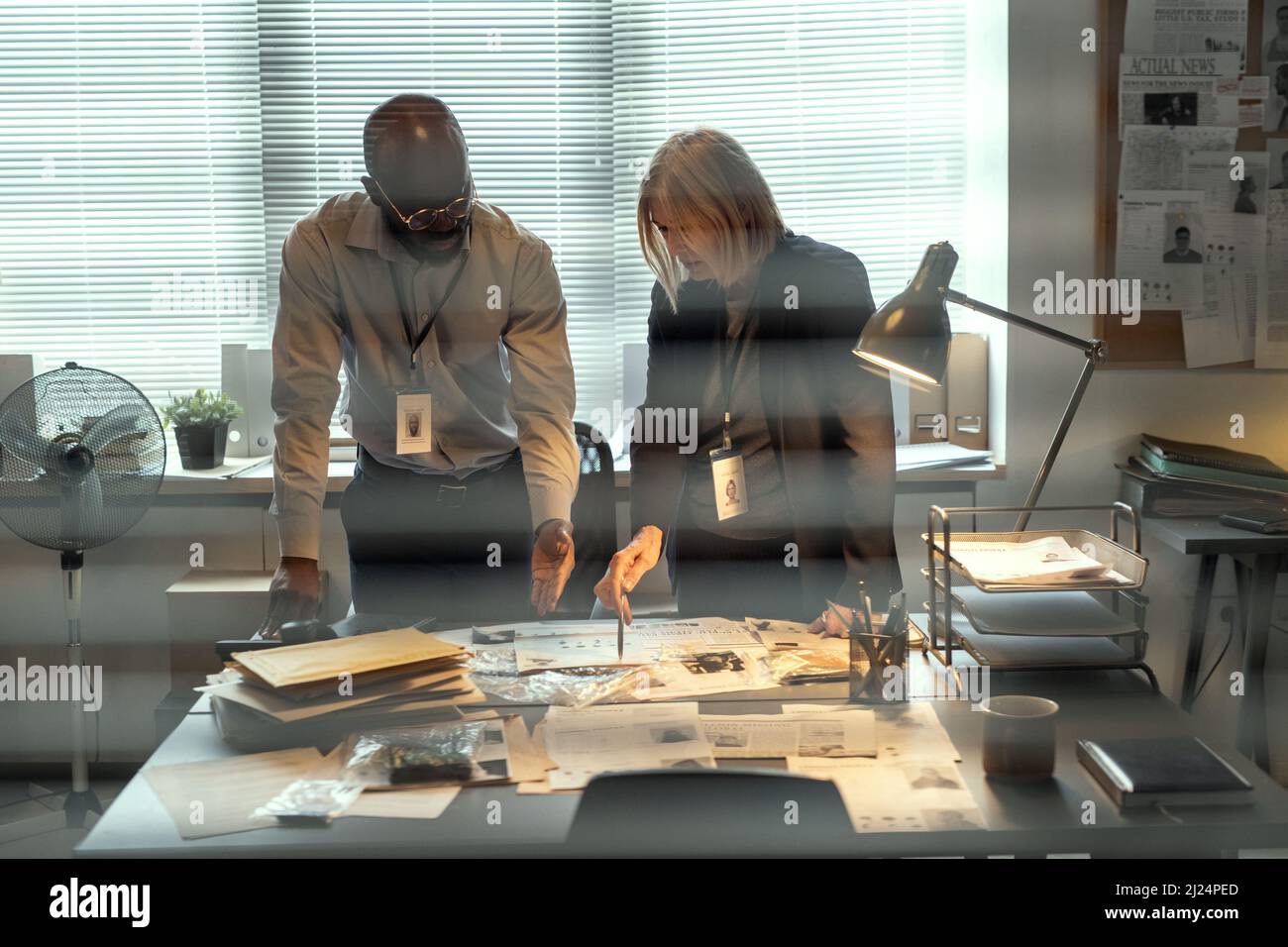 Two confident FBI agents bending over desk with criminal profiles and ...