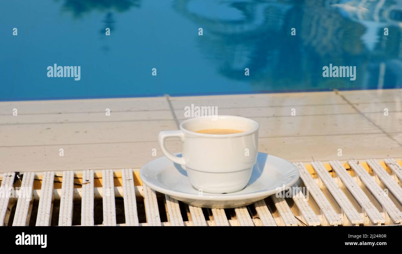 White cup of coffee or hot drink on the background of a blue swimming ...