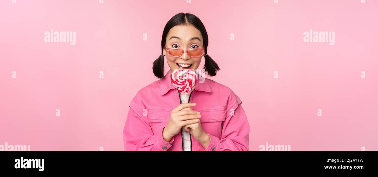 Silly and cute asian female model licking lolipop, eating candy sweet ...