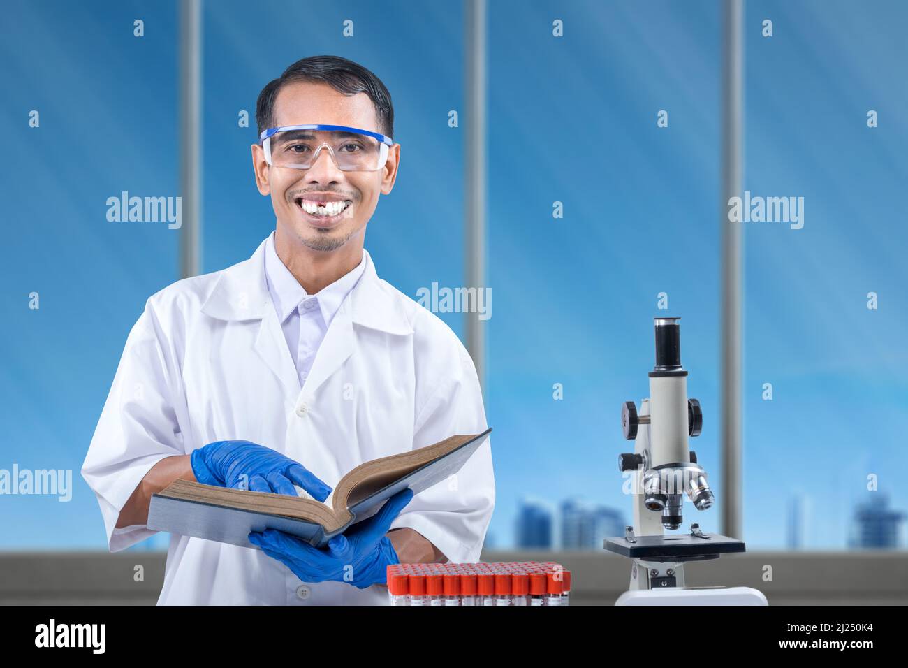 Asian nerd scientist standing and holding a book with a microscope and ...