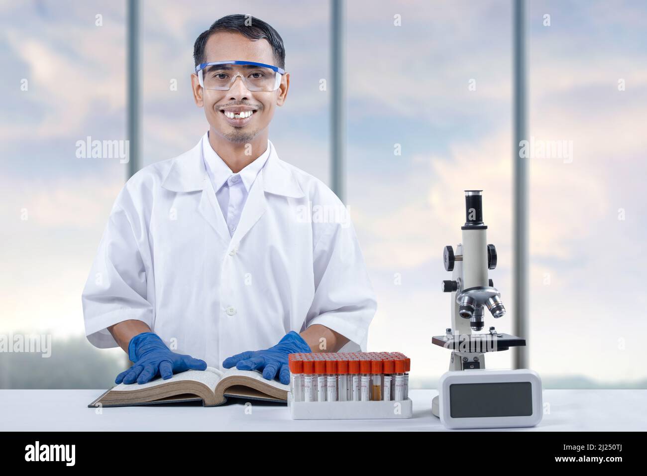 Asian nerd scientist standing and holding a book with a microscope and ...