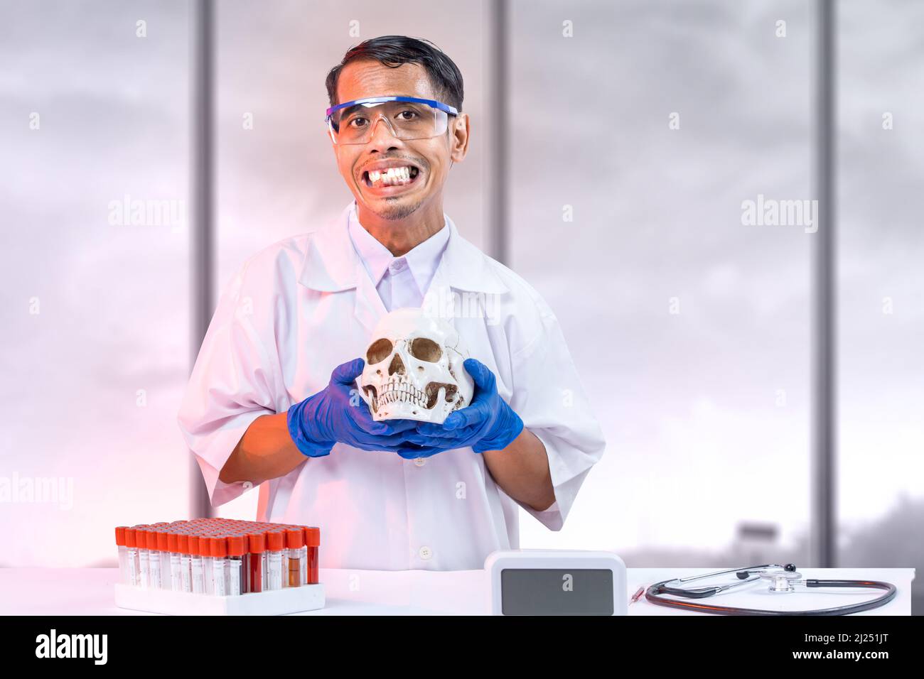 Asian nerd scientist standing and holding a skull head with a ...