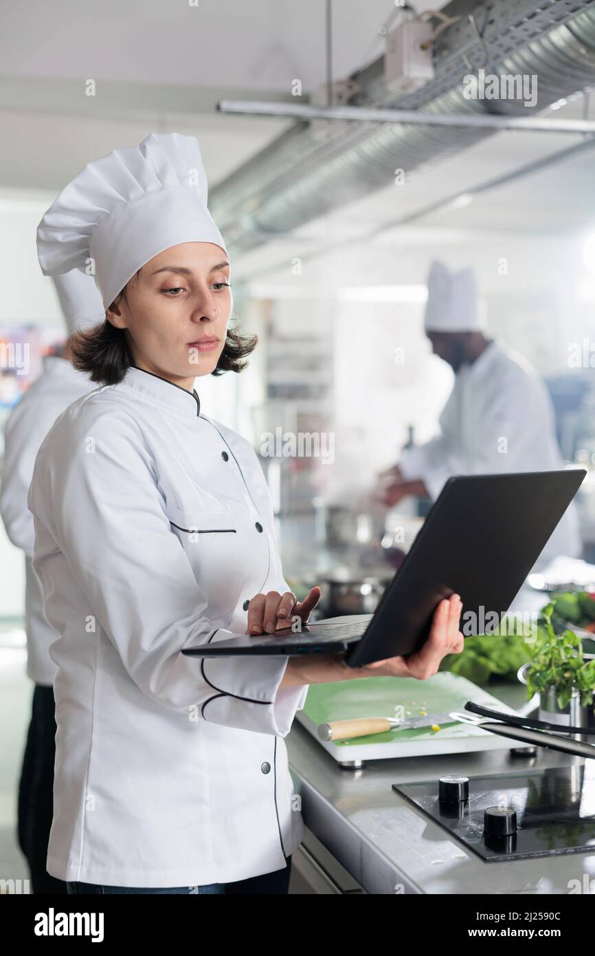 Restaurant kitchen worker with laptop searching gourmet cuisine dinner ...