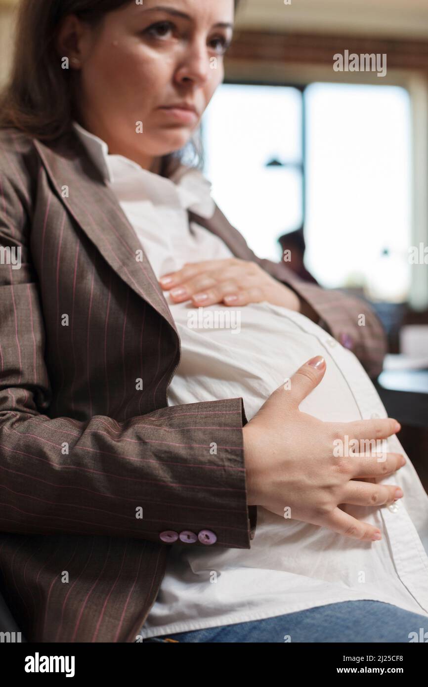 Close up of pregnant woman touching pregnancy tummy while in agency ...