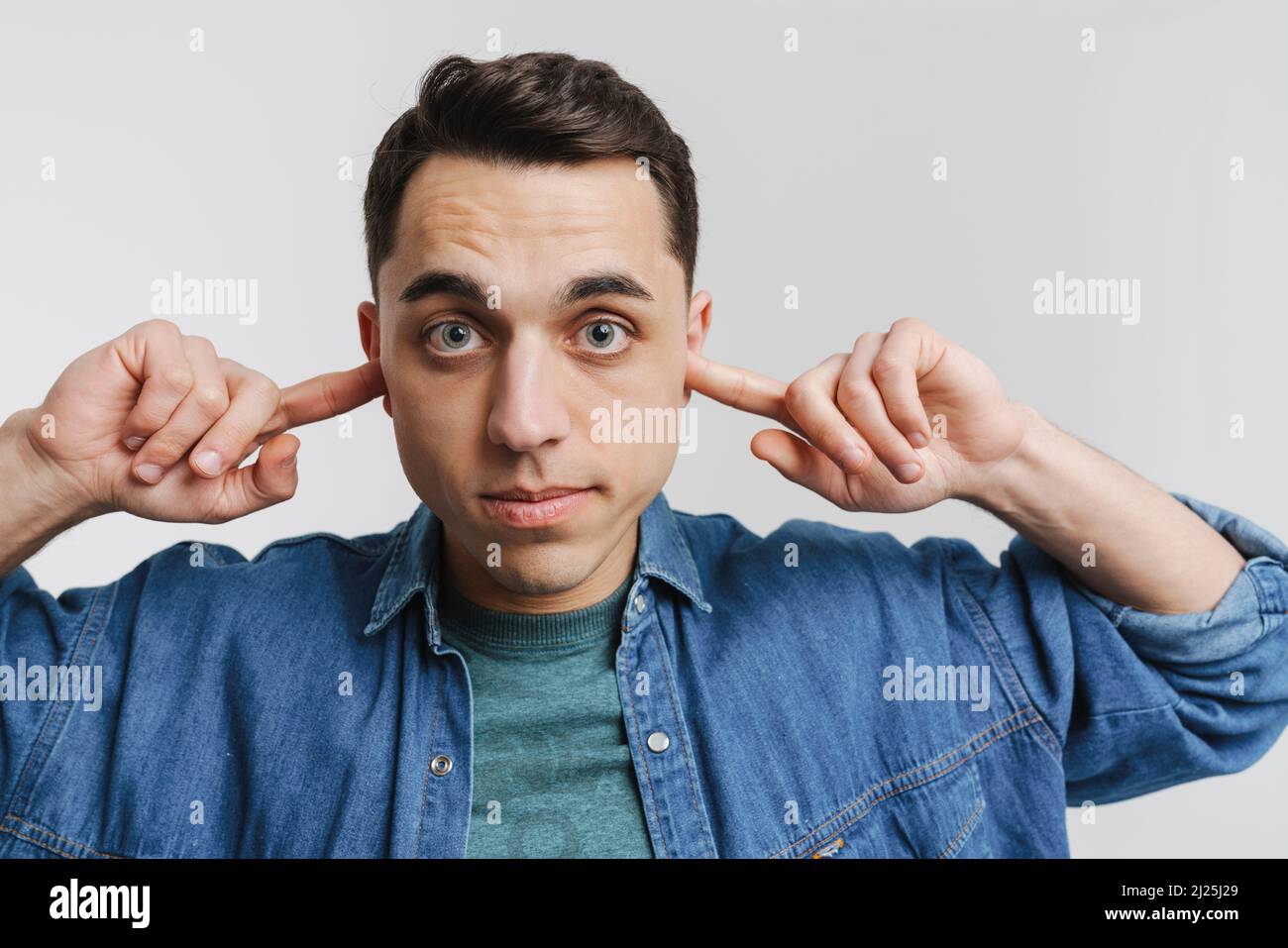Young brunette man looking at camera and plugging his ears isolated ...
