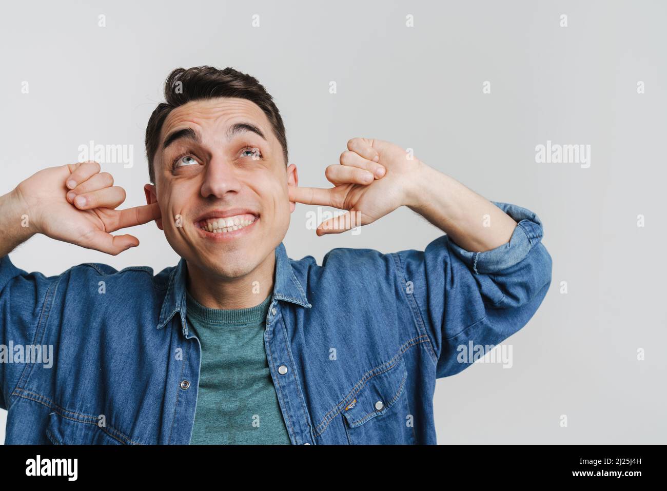 Young brunette man smiling and plugging his ears isolated over white ...