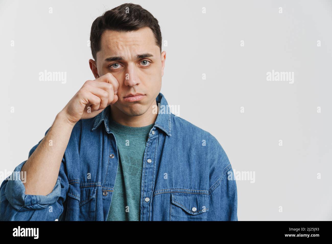 Young brunette man wiping her tears while crying at camera isolated ...