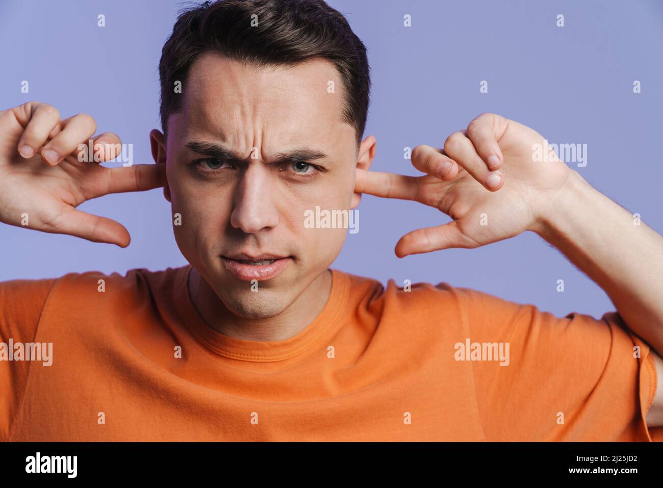 Young brunette man frowning and plugging his ears isolated over purple ...