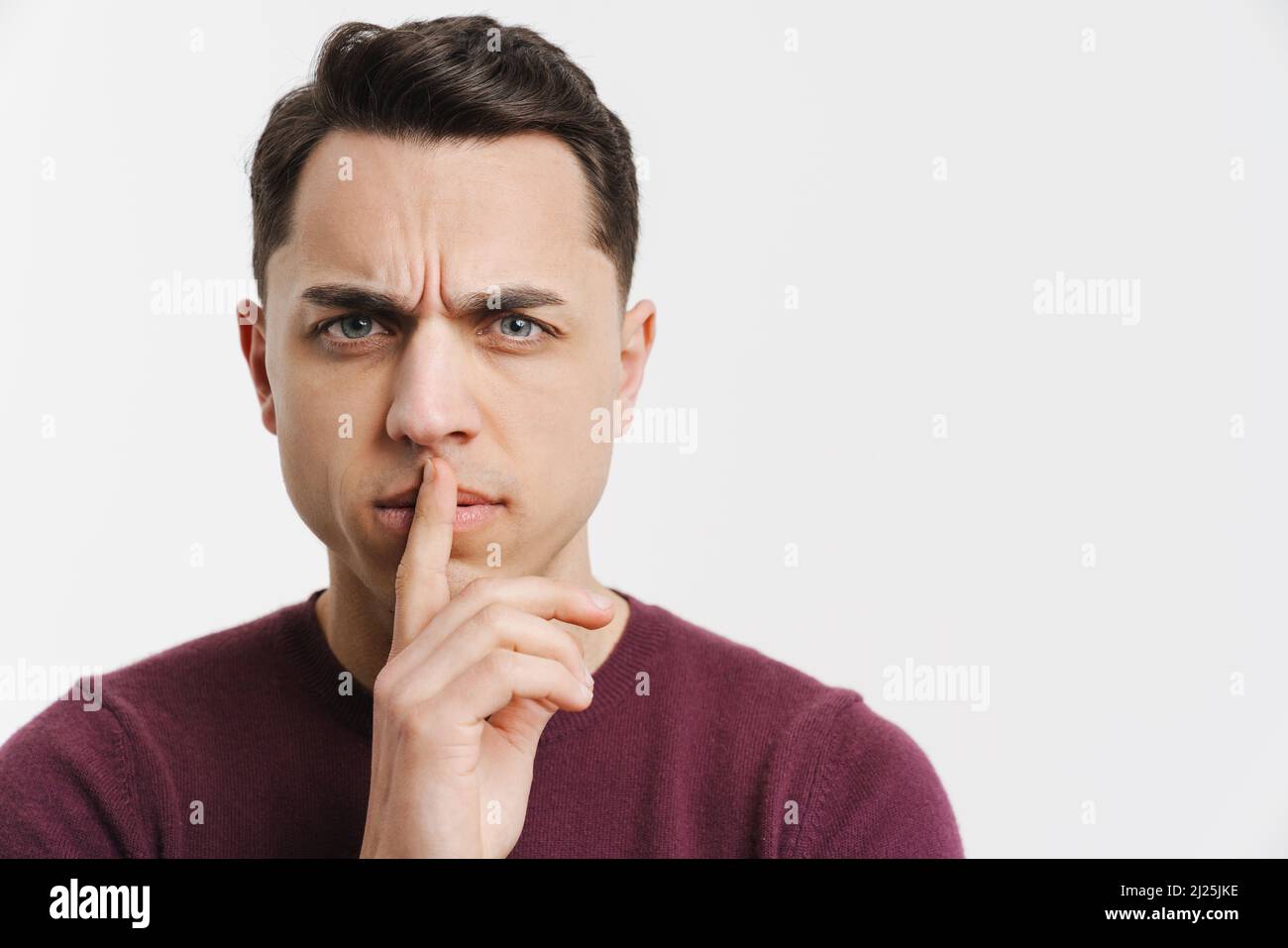 Young white man frowning and showing silence gesture at camera isolated ...