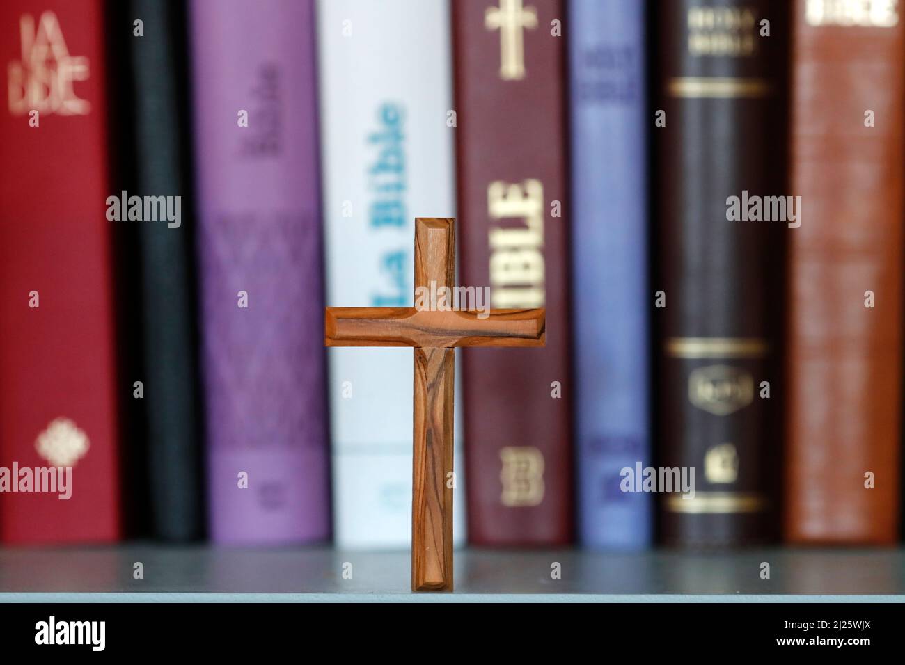 Wooden cross and Christian bibles of different versions on a bookshelf ...