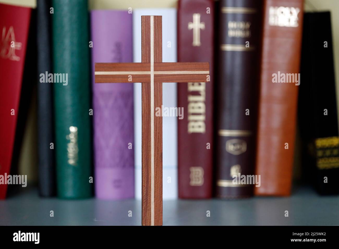 Wooden cross and Christian bibles of different versions on a bookshelf ...