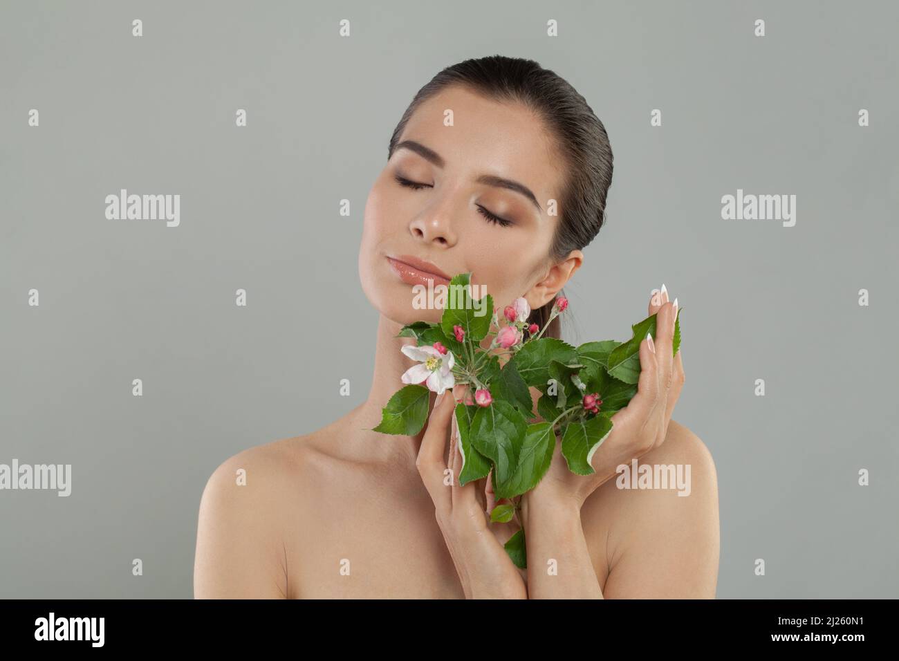 Cheerful beautiful lady spa model with spring flower on grey background ...