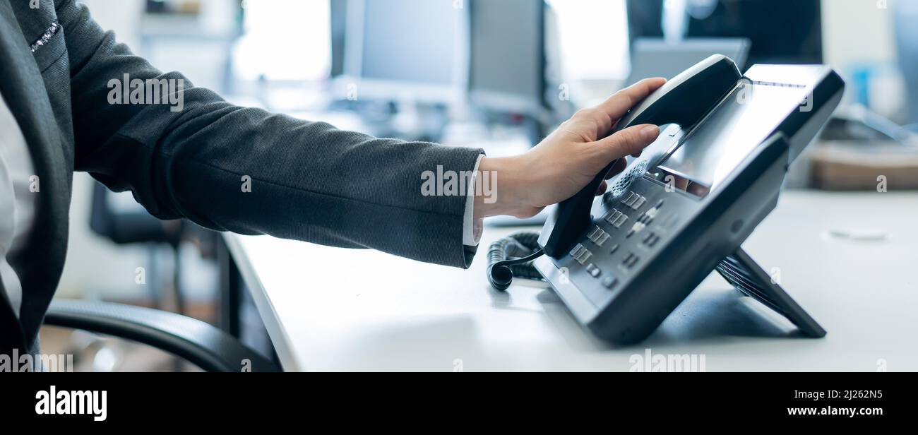 Close-up of a female employee's hand on a landline phone. Woman picks ...