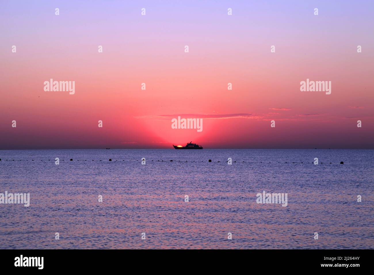A mesmerizing scenery of the pink sunset over the sea with a lonely boat gliding on it Stock ...
