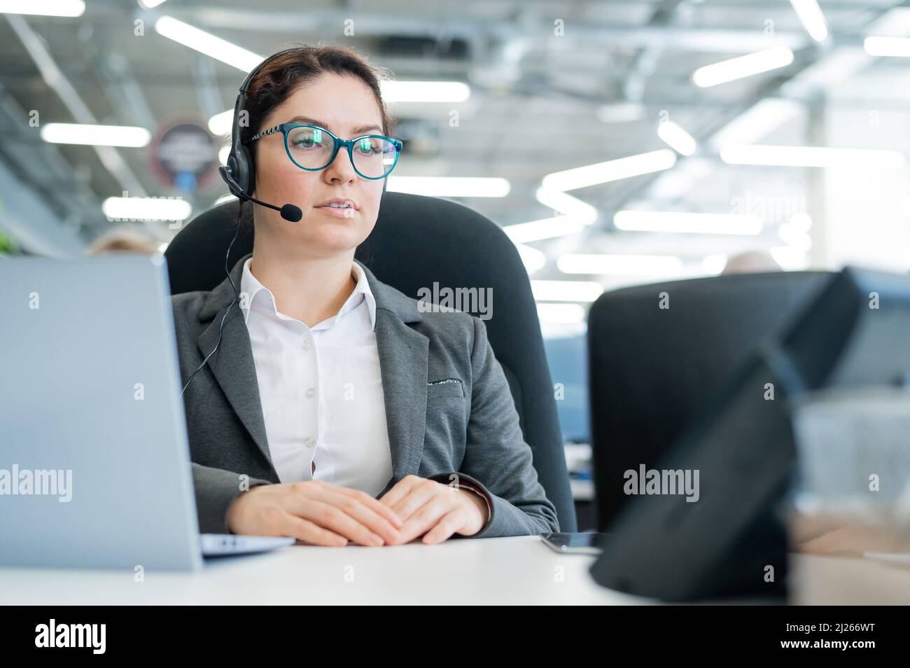 A happy female support operator is sitting at a desk and answering calls. Beautiful smiling ...
