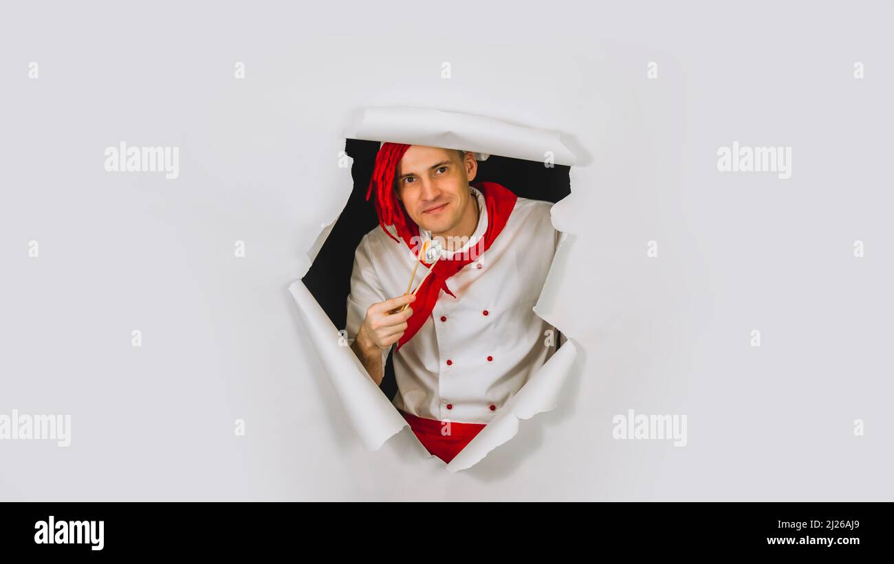 Young man dressed as chef holding chopsticks with roll. Male cook with ...