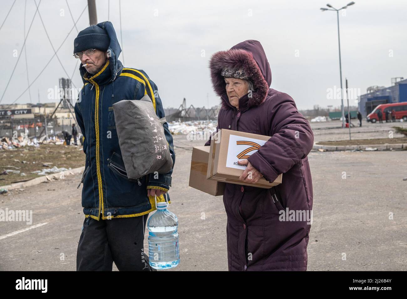 A couple carries Russian humanitarian aid from a destroyed supermarket ...