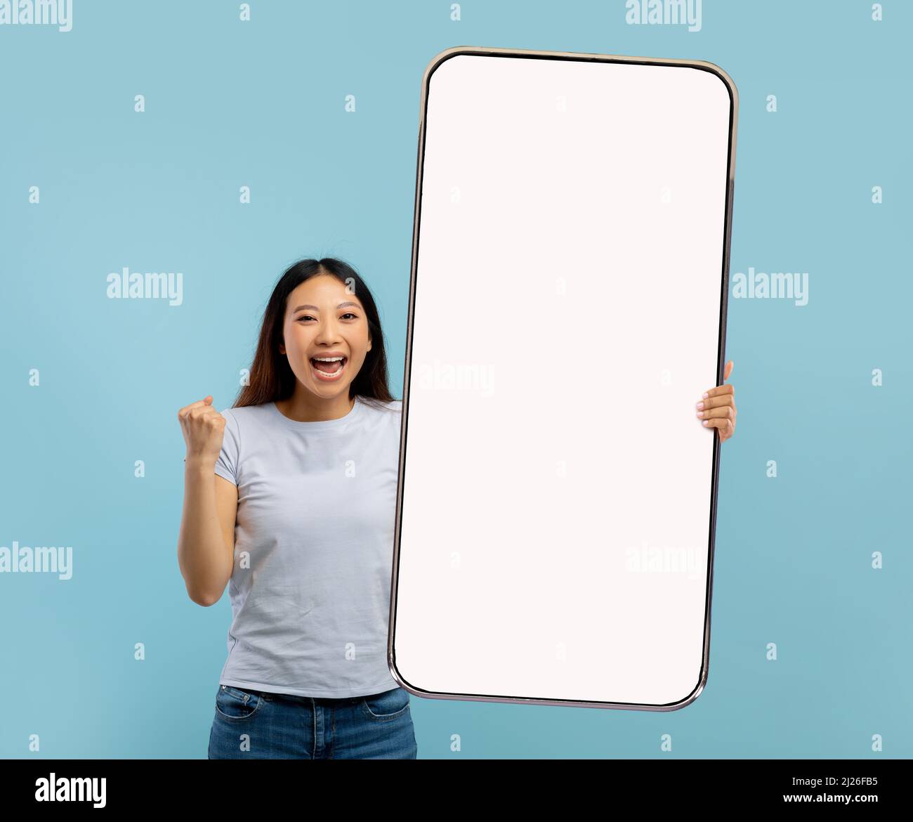 Excited young Asian woman holding big cellphone with empty screen ...