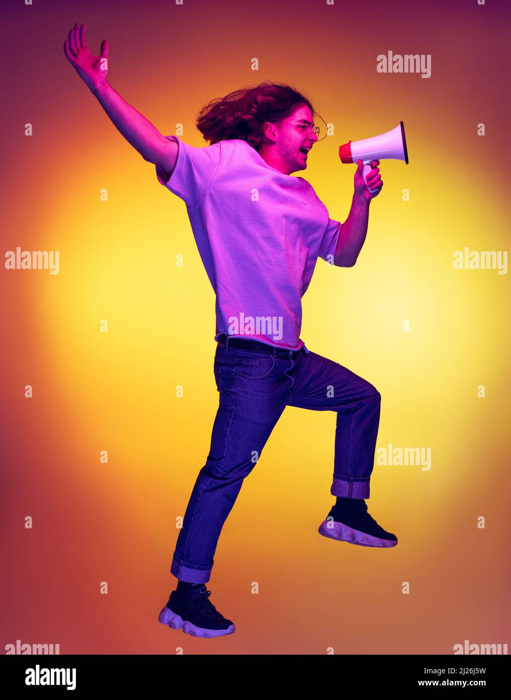 Full-length portrait of young excited man jumping with megaphone ...
