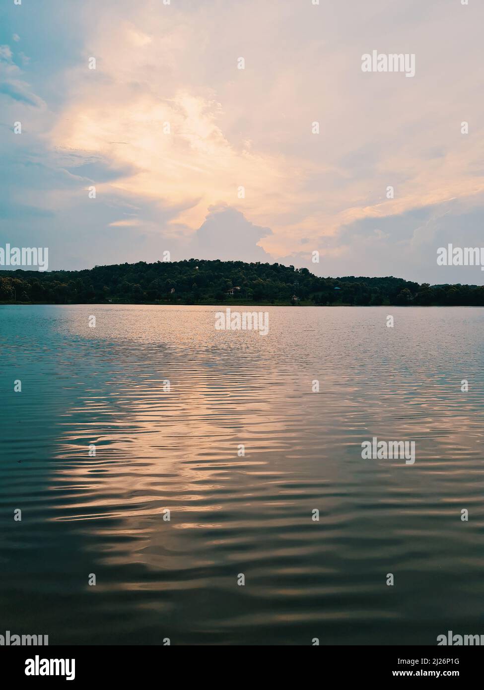 A vertical shot of a light cloudy sunset reflected on a lake with land ...