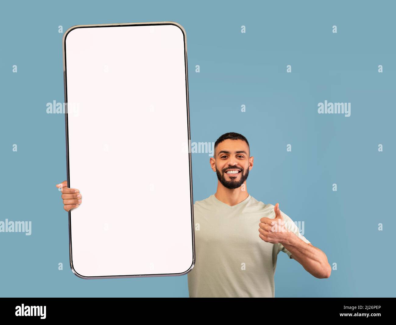 Smiling young Arab man demonstrating giant smartphone with mockup ...