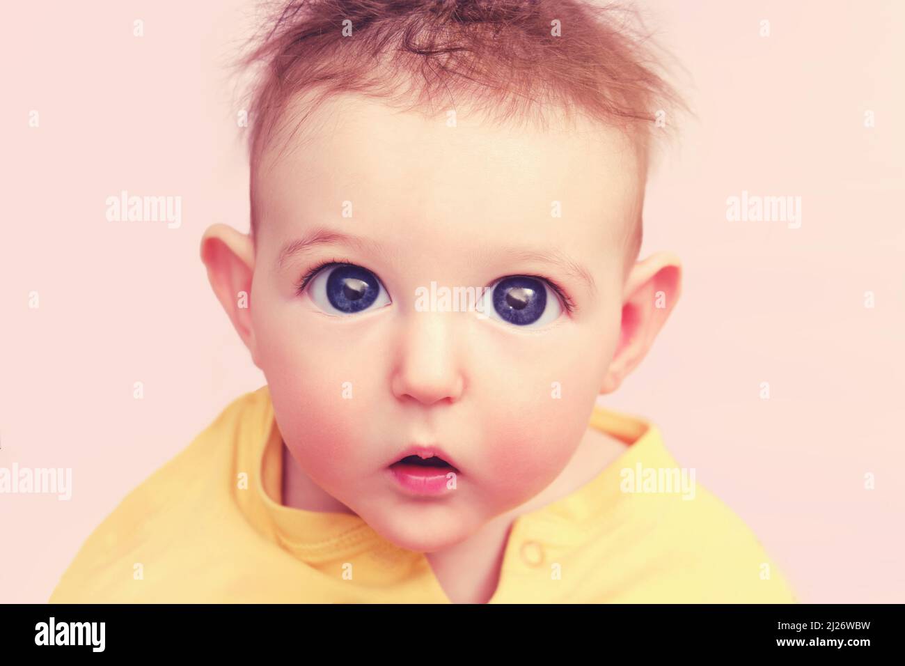 Curious toddler baby boy with big eyes on a pink background, face close ...