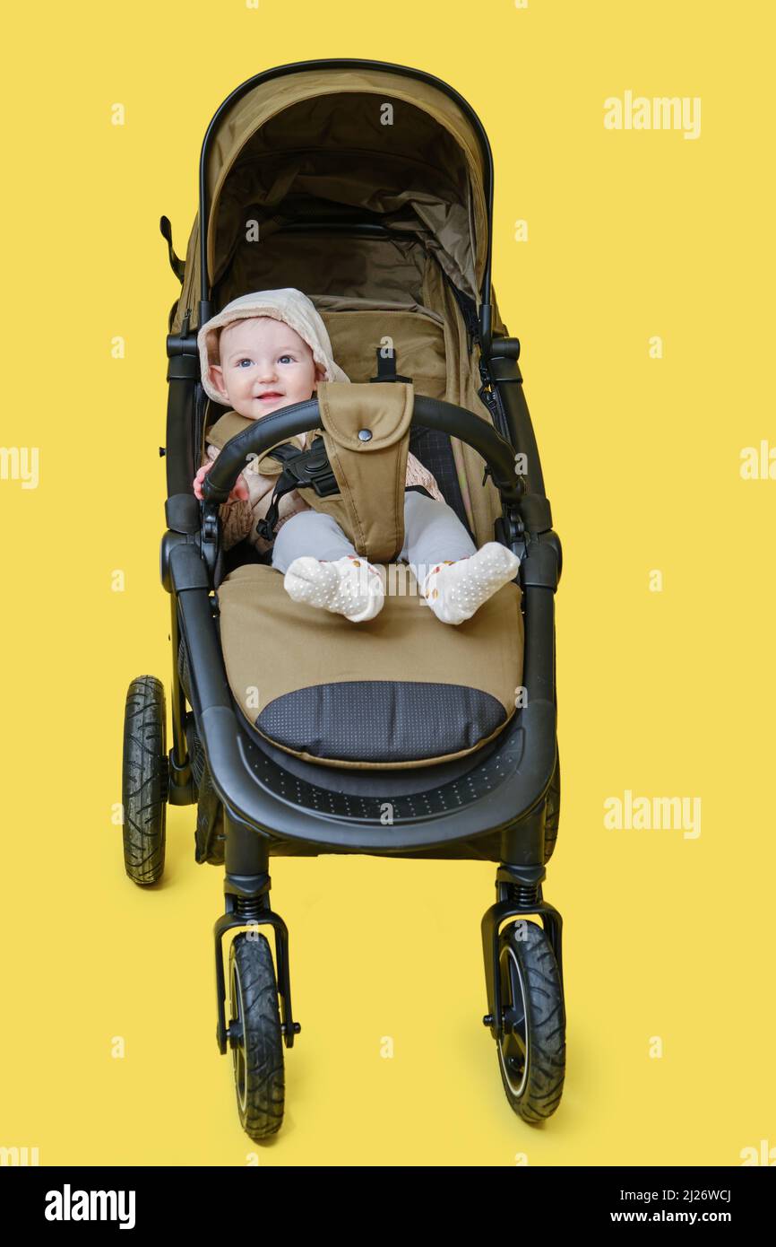 A happy child is sitting in a baby carriage on a studio yellow ...