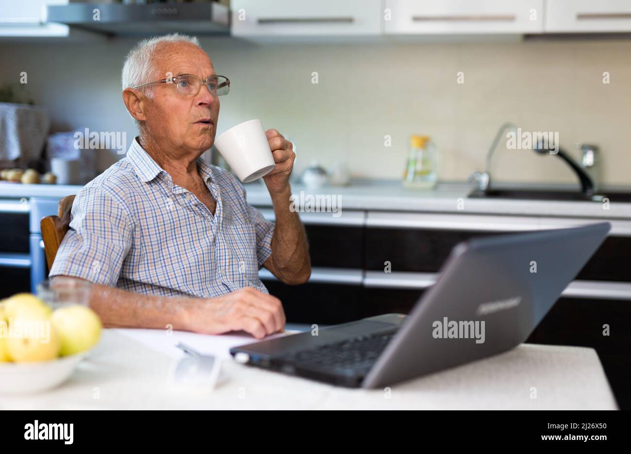 Old man sitting in kitchen at table with laptop Stock Photo - Alamy
