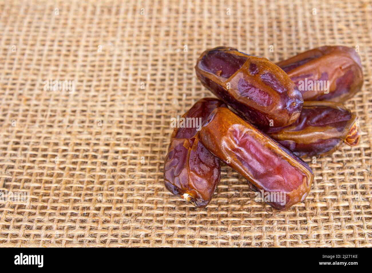 Dried dates. Stack of date fruits on burlap background. Space for text ...