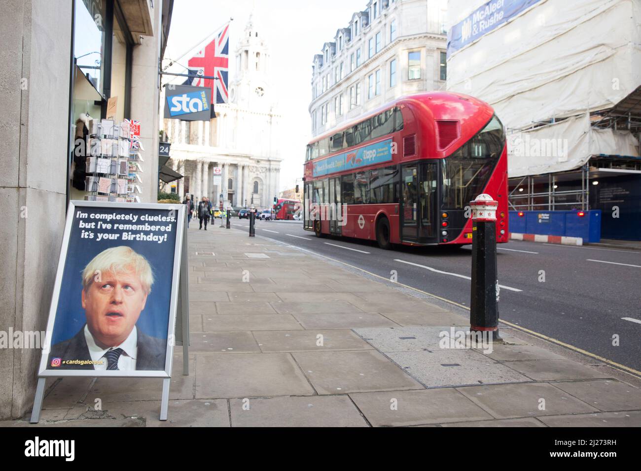A double-decker bus runs past a signboard featuring Britain's Prime ...