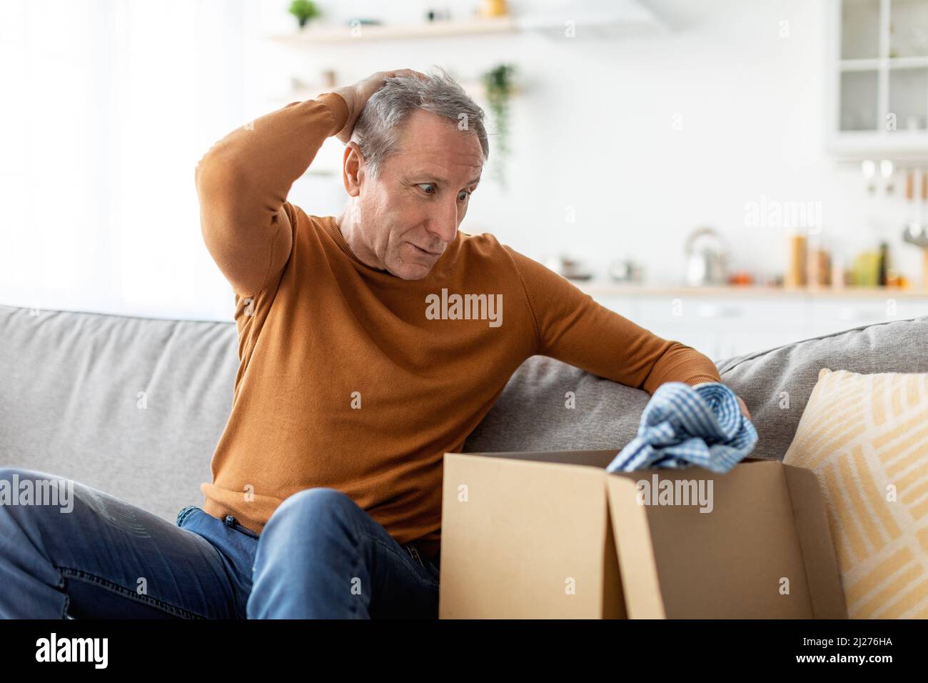 Confused mature man unpacking wrong parcel, delivery mistake concept ...
