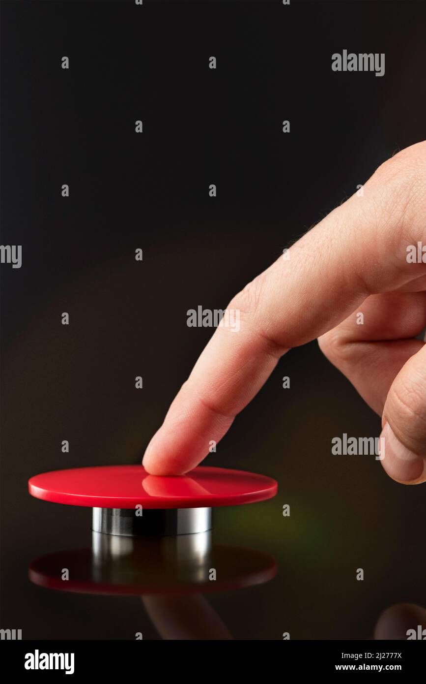 A man's hand presses a big red button. Red button on a dark background ...