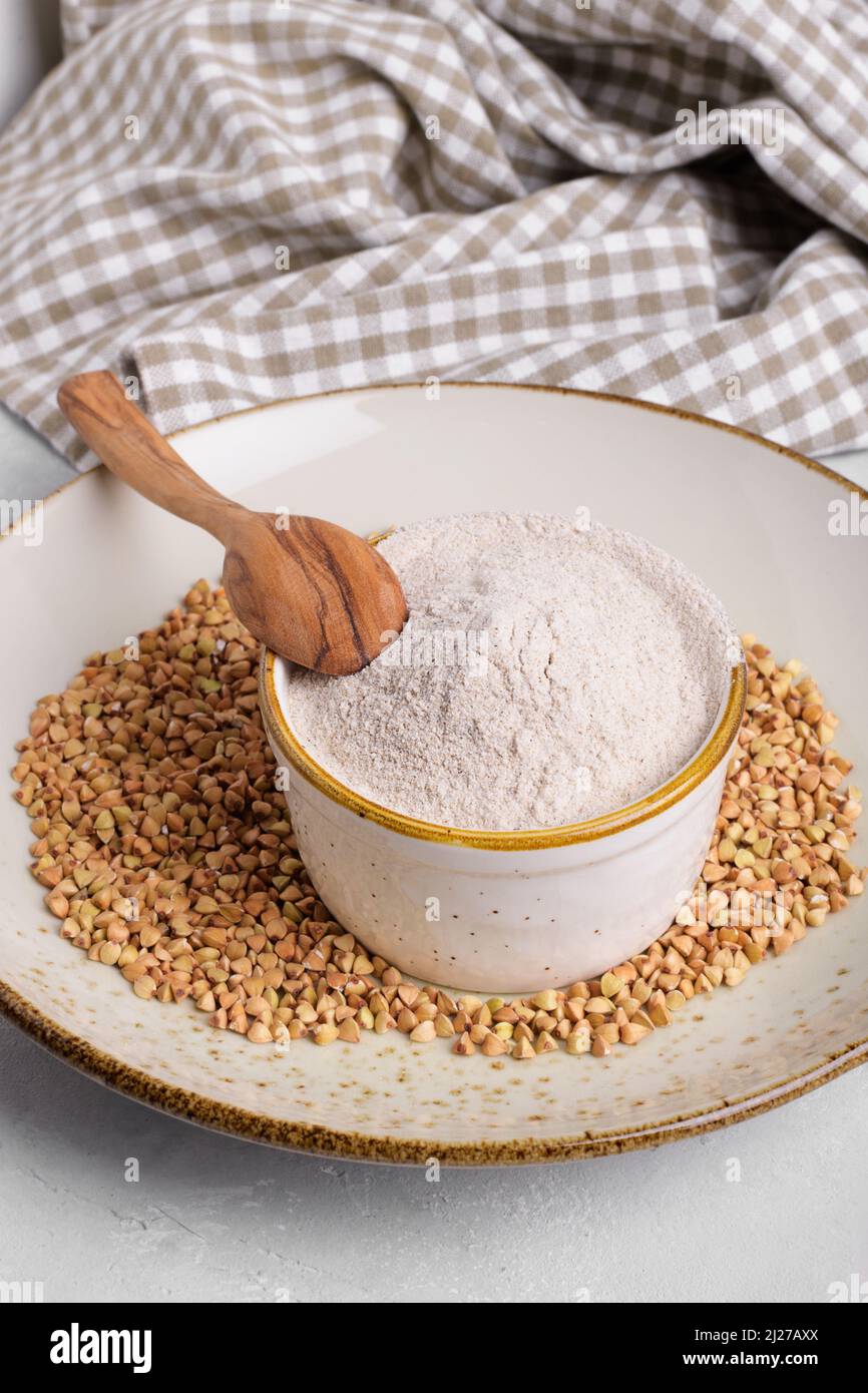 Buckwheat flour in a ceramic bowl with spoon and raw green buckwheat ...