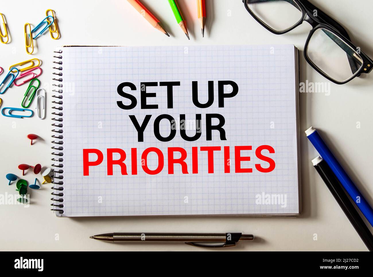 Laptop, red pen and notepad with text Set up your priorities in the ...