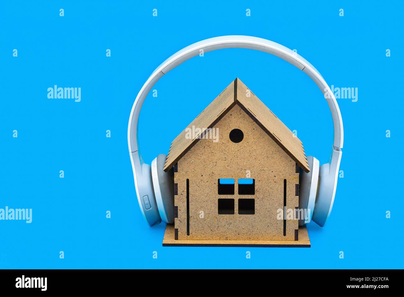 Wireless overhead headphones on a wooden house model isolated on a blue ...