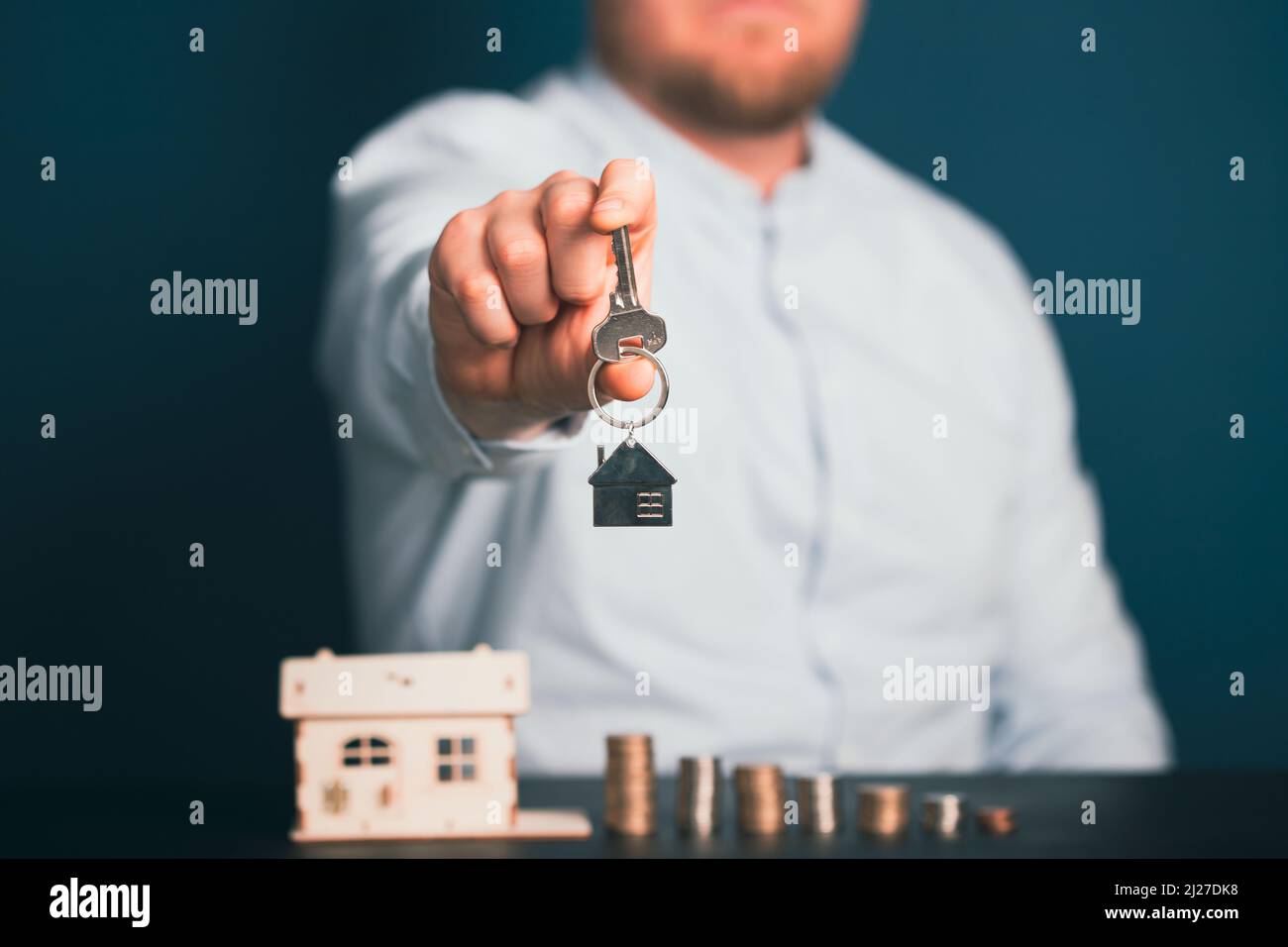 Real estate agent hand holding key near a pile of coins and . Realtor ...