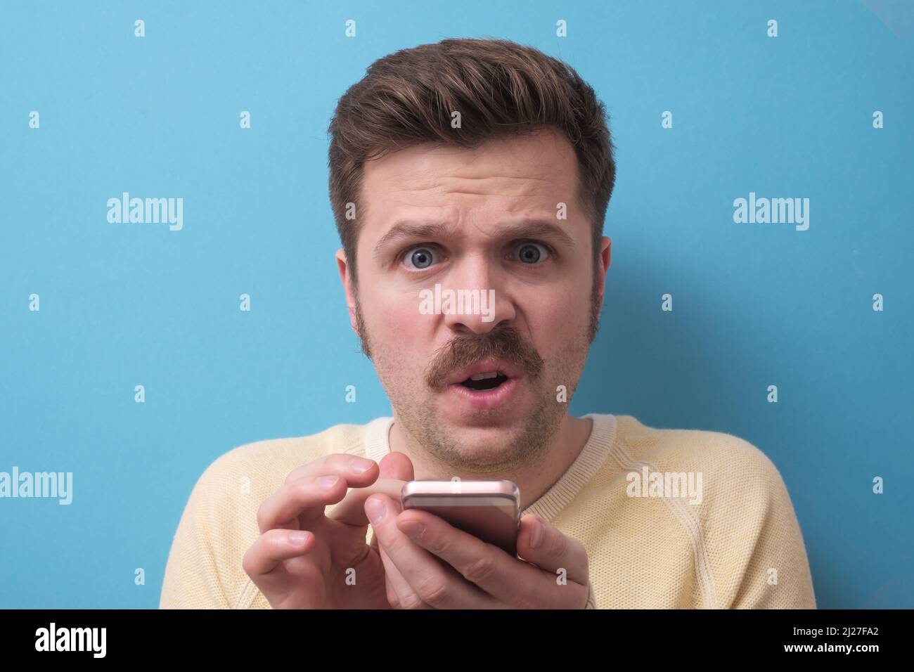 Amazed young guy reads a message on the phone. Shocked and surprised ...