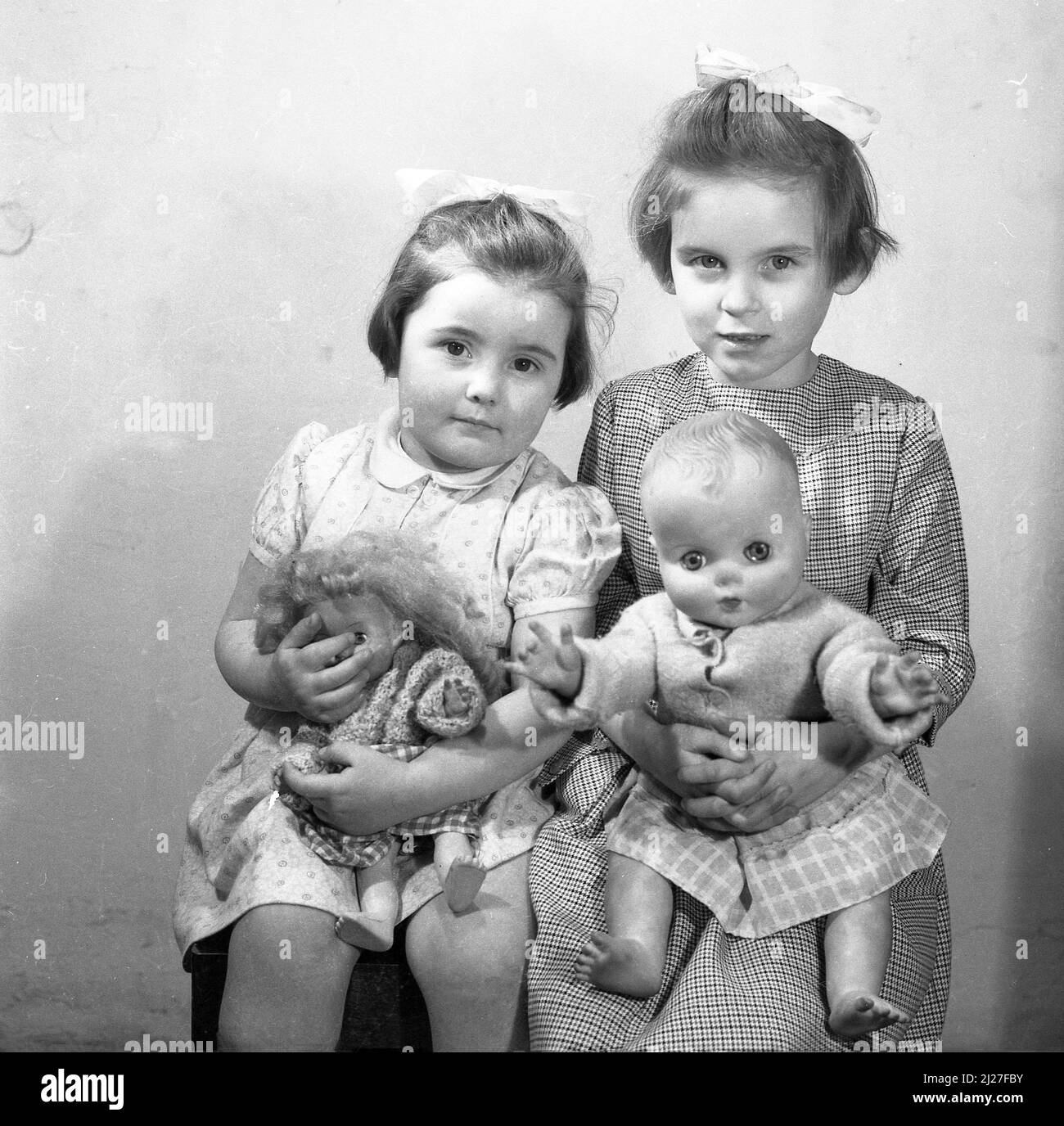 1960, historical, two young girls, sisters, holding their toy dolls as ... 1960, historical, two young girls, sisters, holding their toy dolls as ...