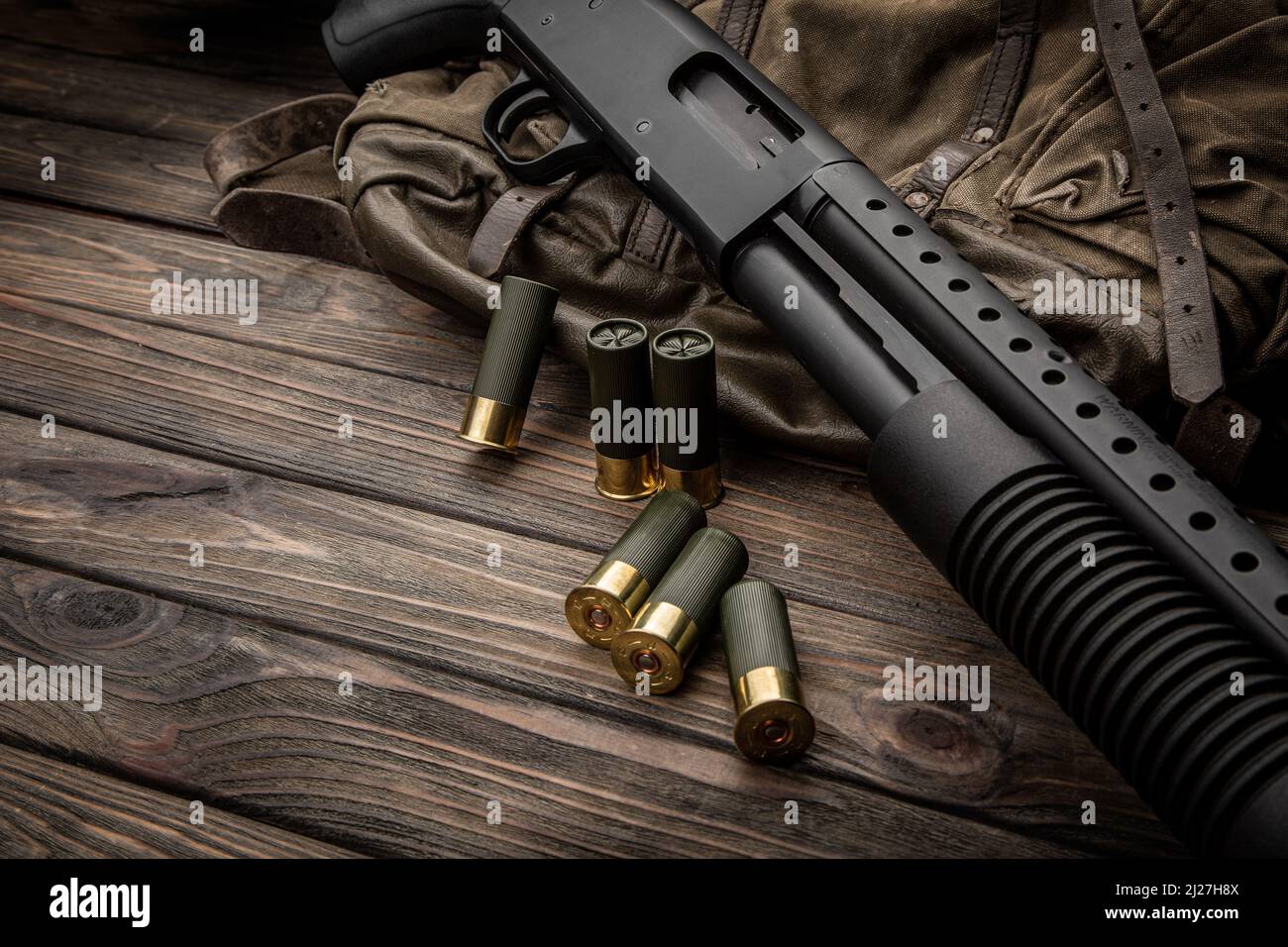 A black 12-gauge pump-action shotgun and ammo are on a canvas backpack ...