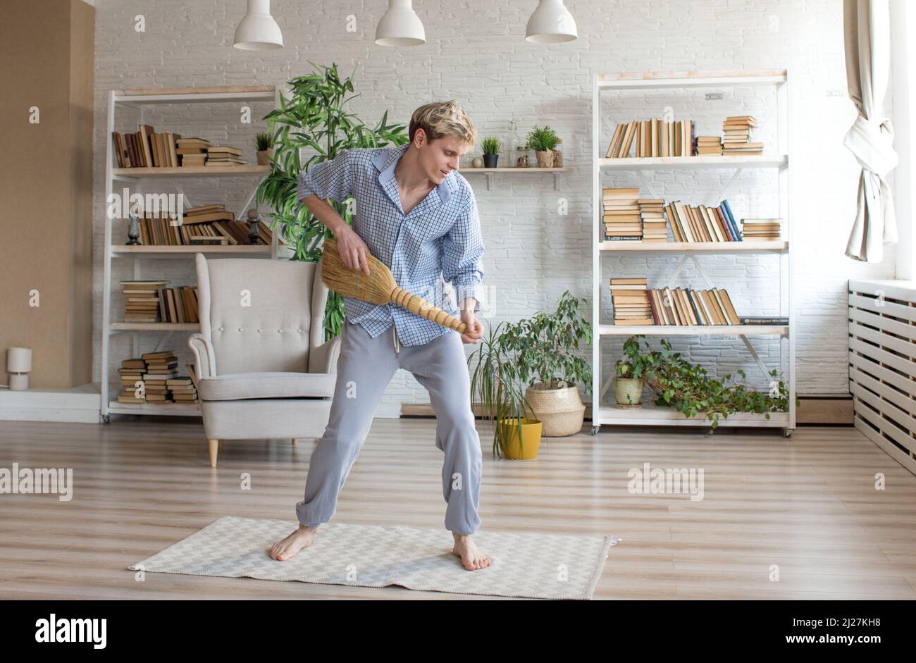 a young happy man sings and dances with a cleaning broom in a large ...