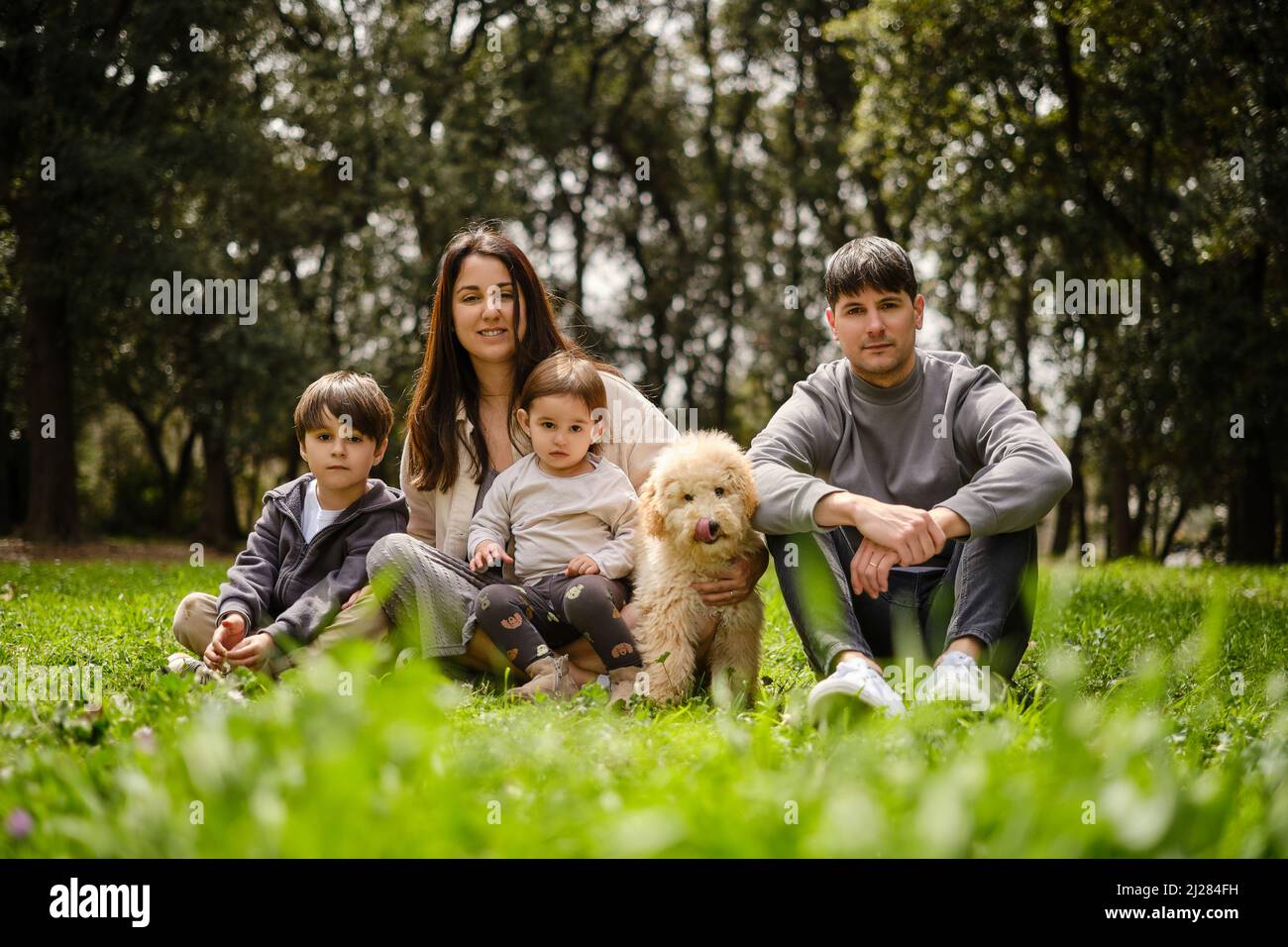 Portrait of a family and dog sitting together on the grass while ...