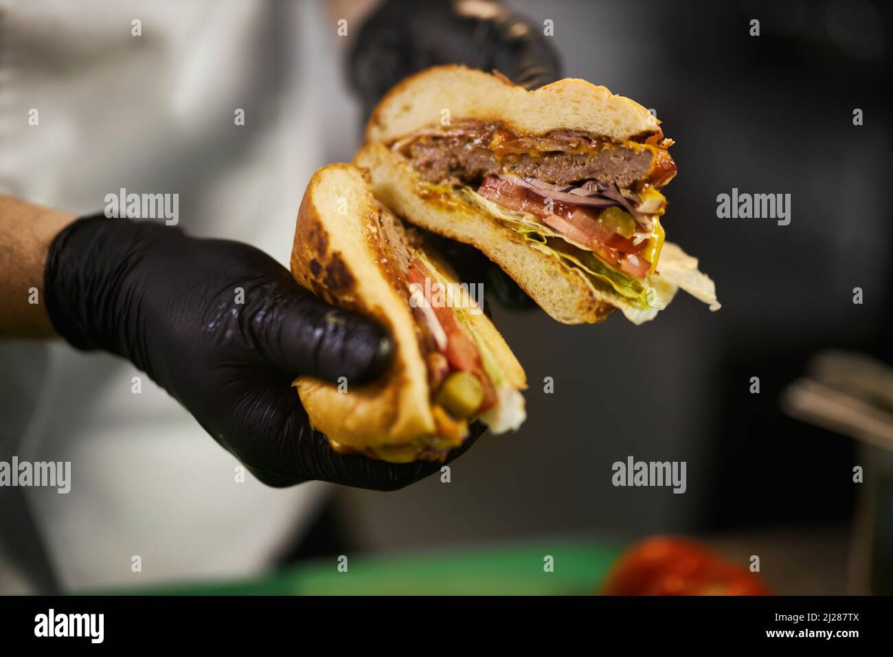 Crop view of male hands holding cut on half beef burgers with cheese ...