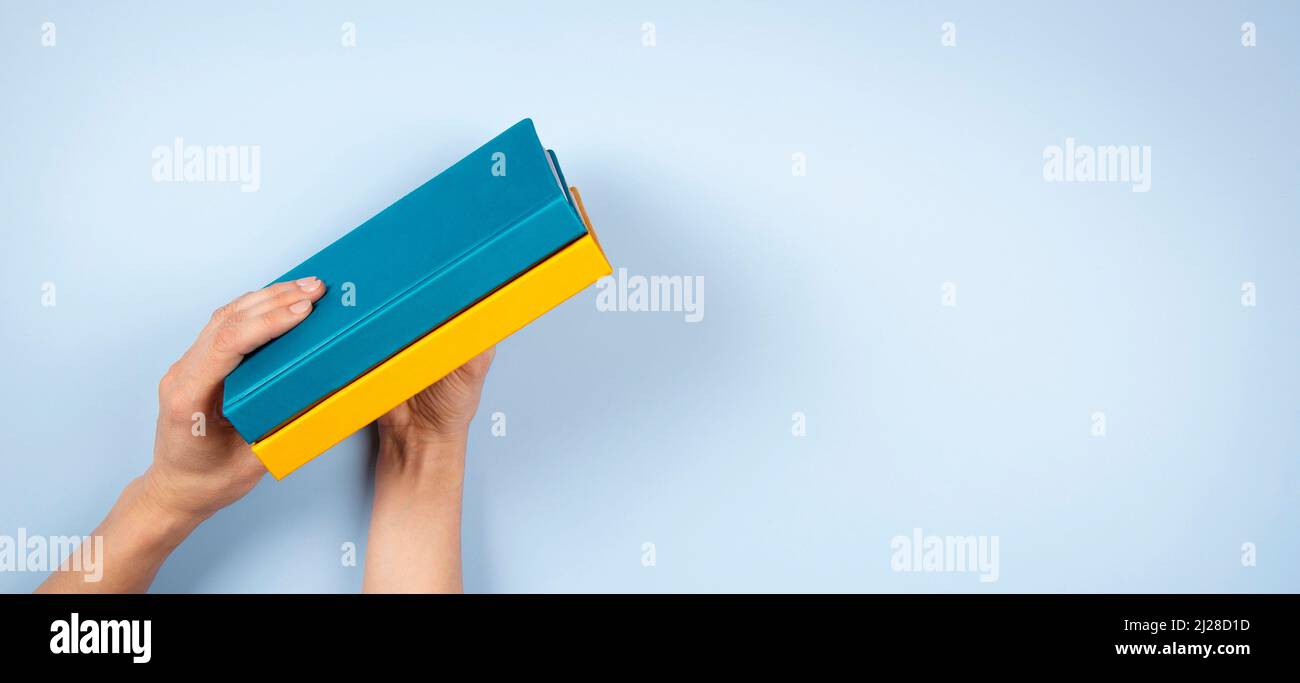 Female hands holding two blue and yellow color books over light blue ...
