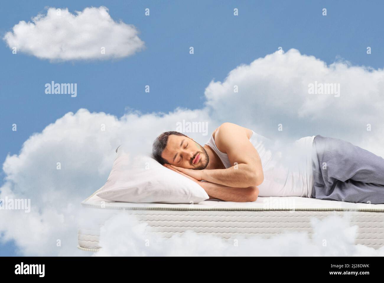 Young man in pajamas sleeping on a mattress and floating on clouds ...