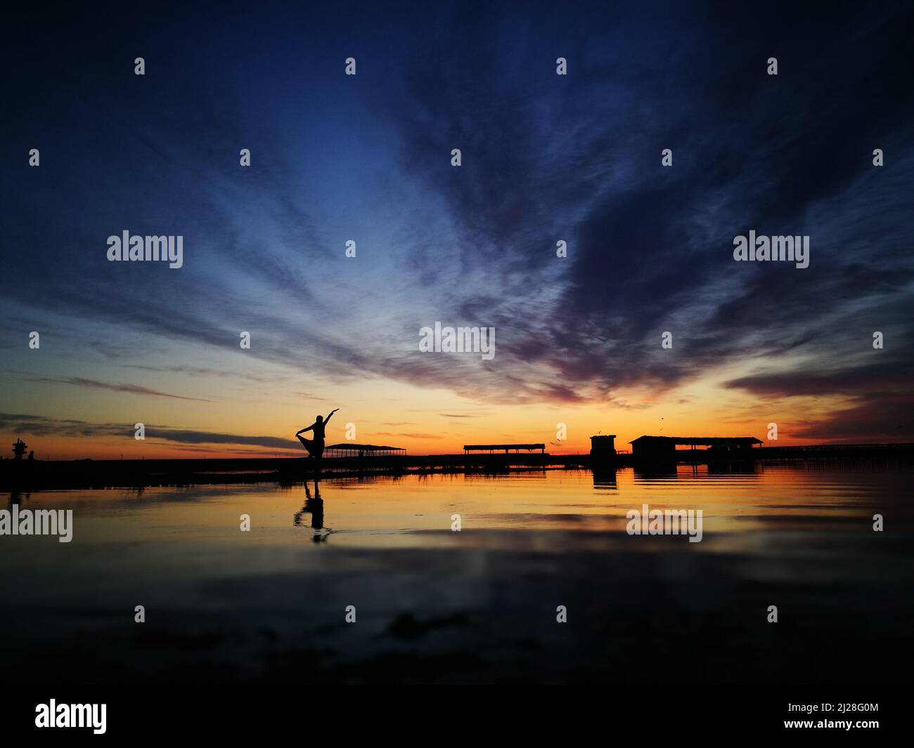A silhouette of a woman dancing under the colorful cloud by the lake ...