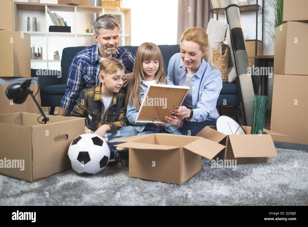 Happy Caucasian family sitting together on floor and unpacking boxes ...