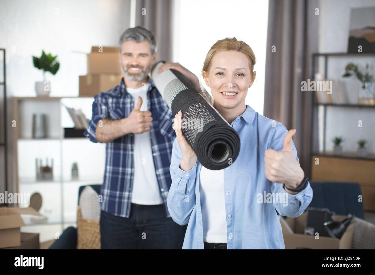 Smiling Caucasian couple carrying rolled rug after moving in a house ...