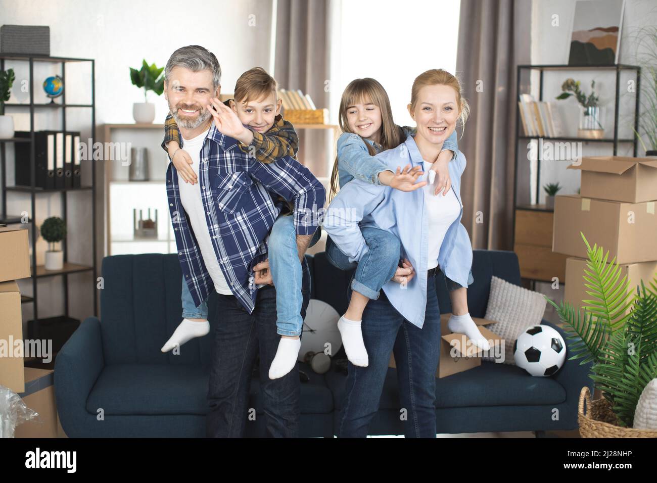 Happy parents piggybacking son and daughter at home. Smiling father and ...