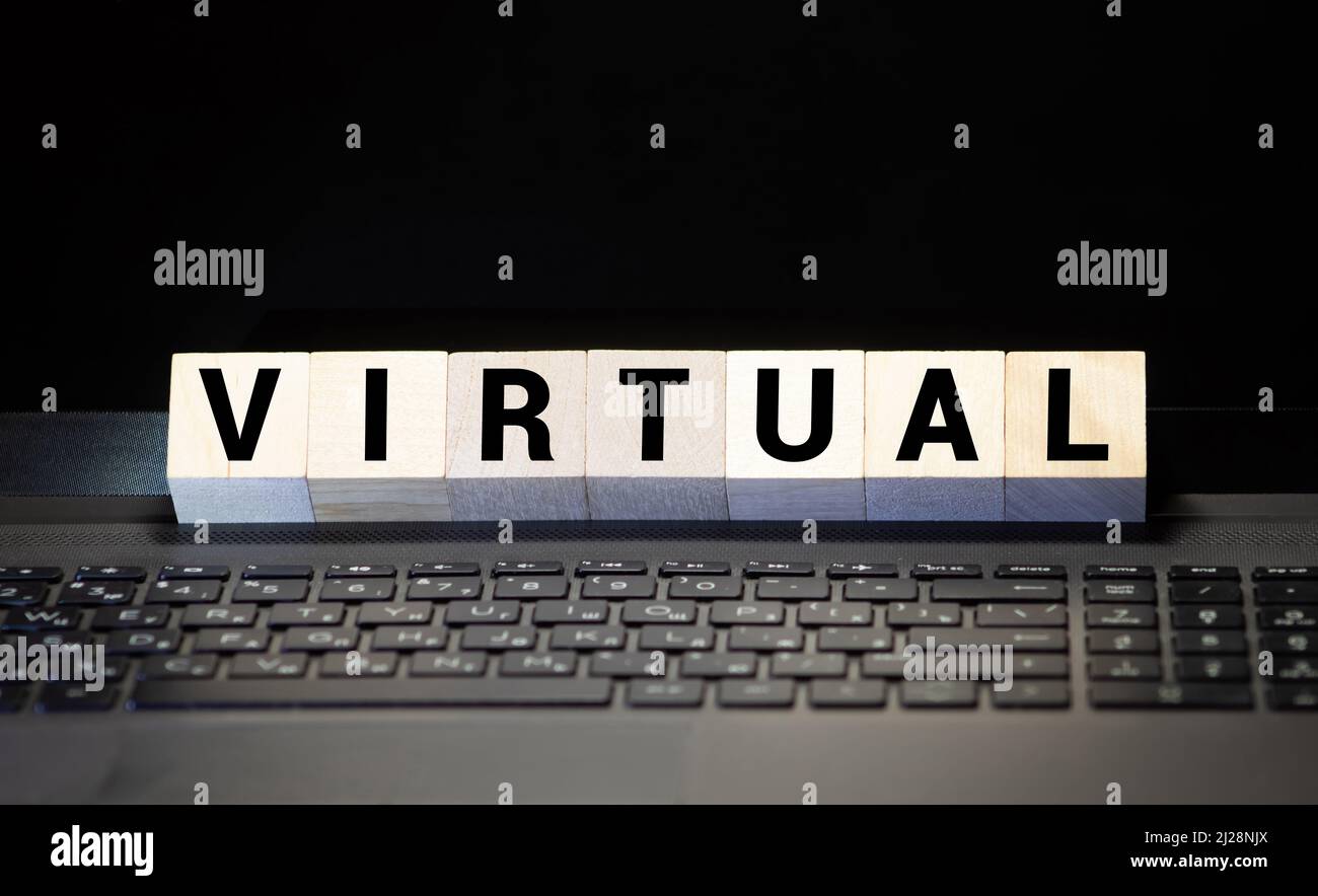 The word VIRTUAL is written on a wooden block on a computer keyboard ...